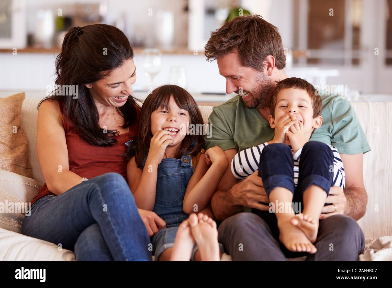 Mid adult white couple and their two young children sitting on a sofa ...