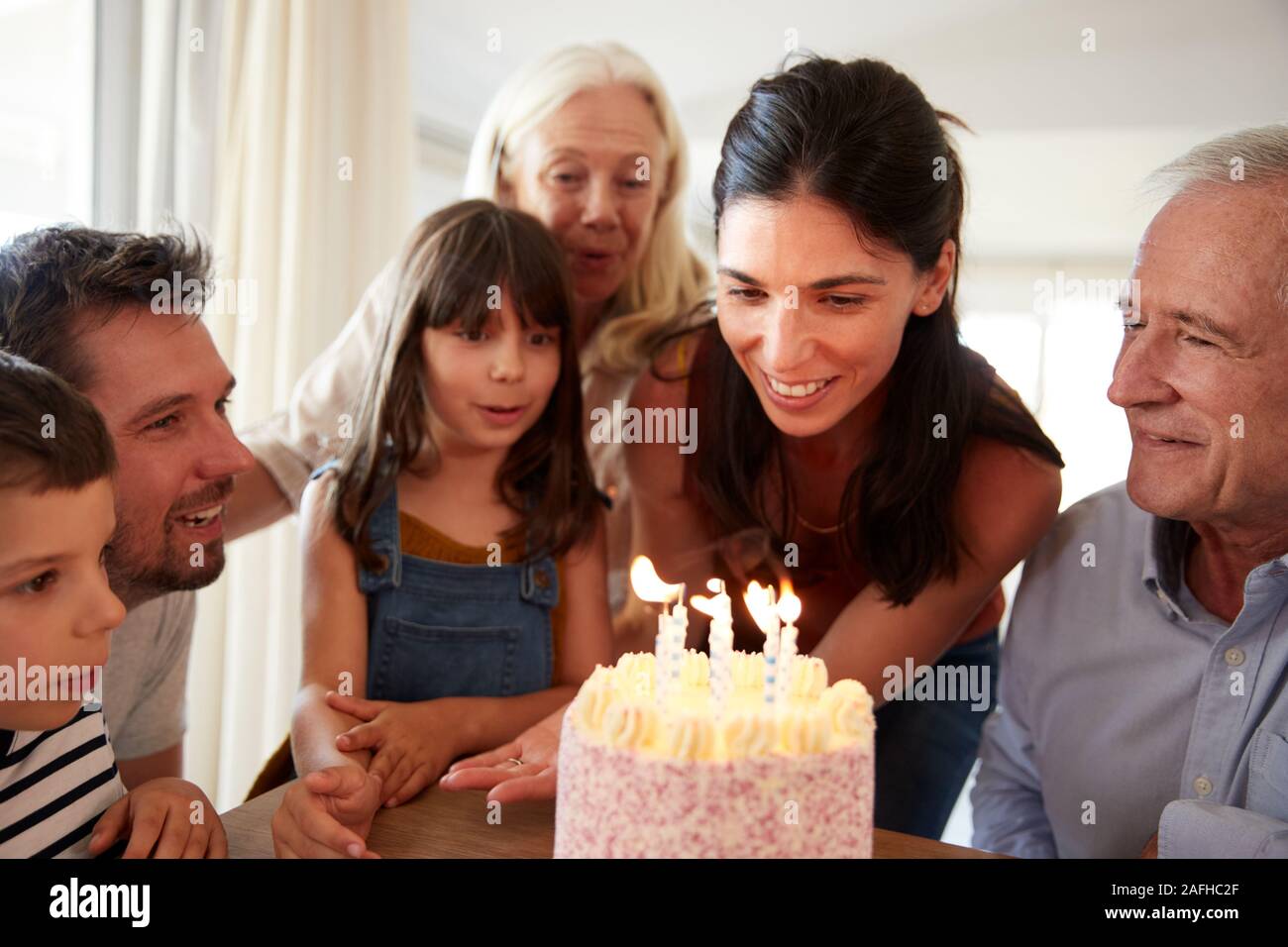 Six year old girl blowing out the candles on birthday cake watched by ...