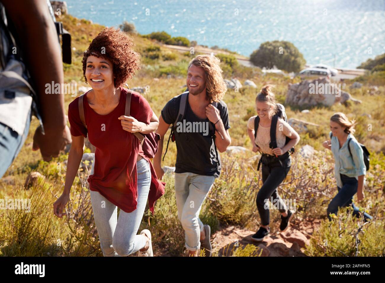 Happy young adult friends hiking single file uphill on a path by the ...