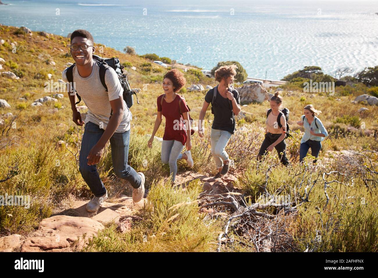 Happy young adult friends hiking single file uphill on a path by the ...