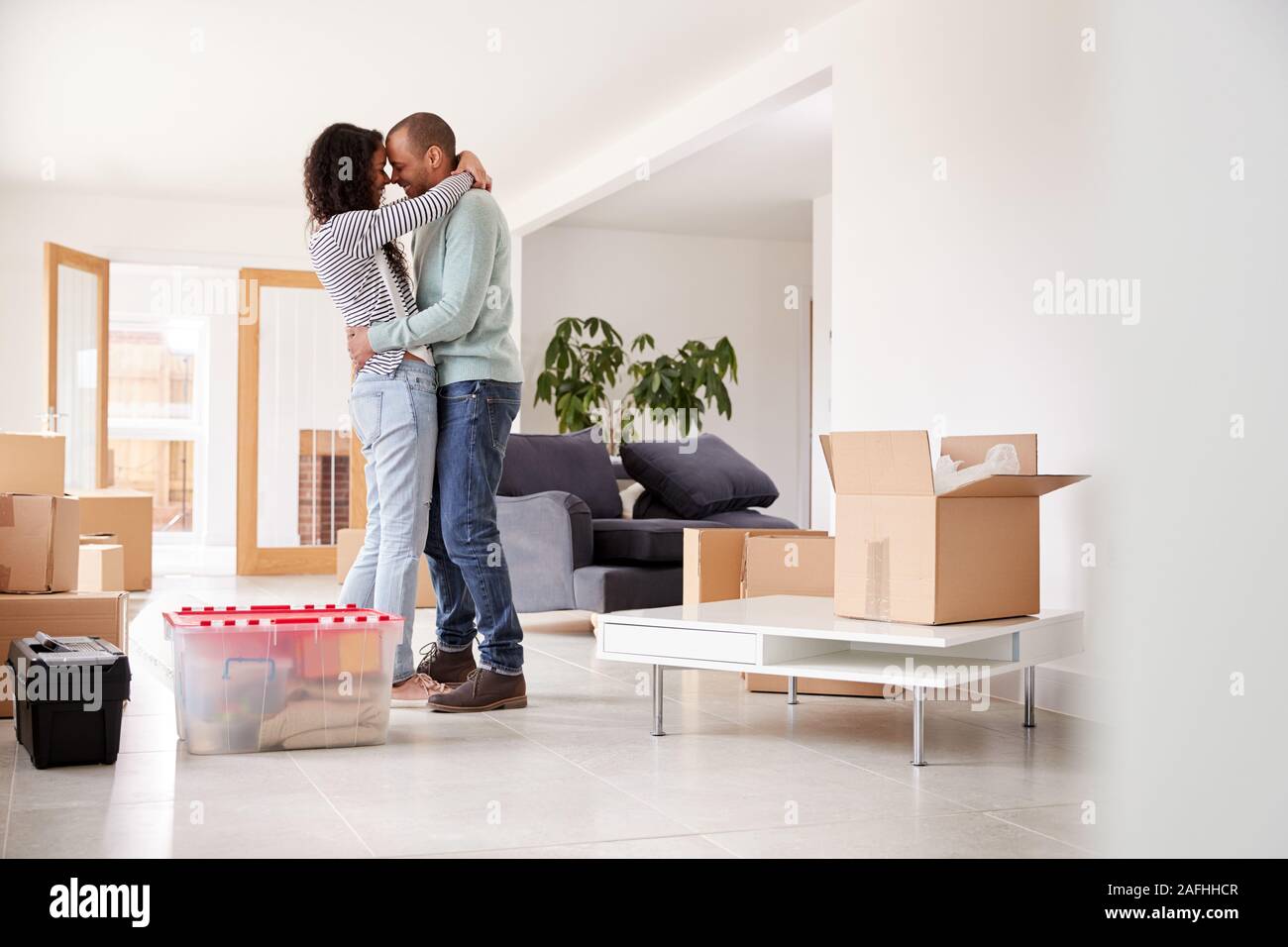 Loving Couple Hugging Surrounded By Boxes In New Home On Moving Day ...