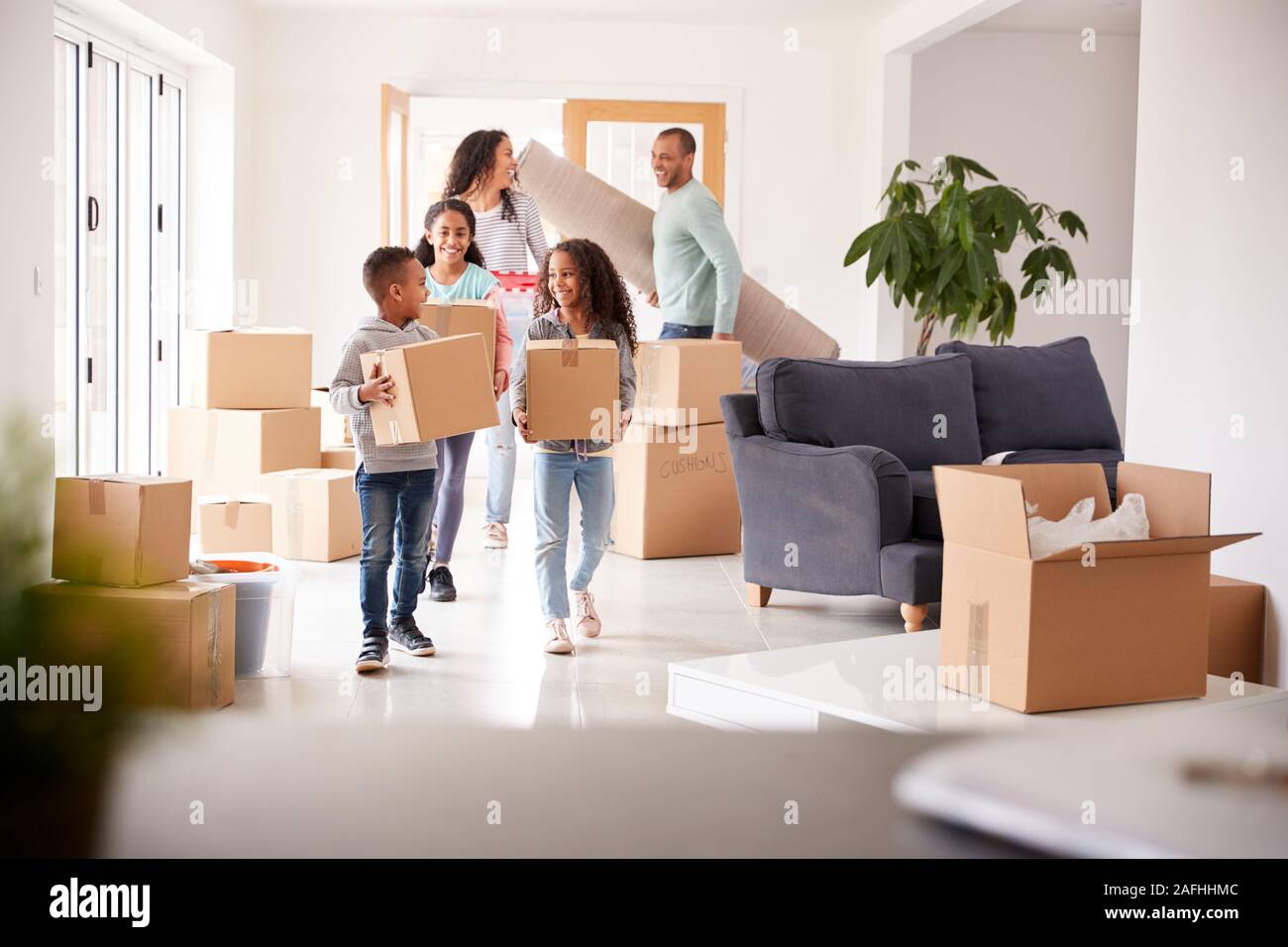 Smiling Family Carrying Boxes Into New Home On Moving Day Stock Photo ...
