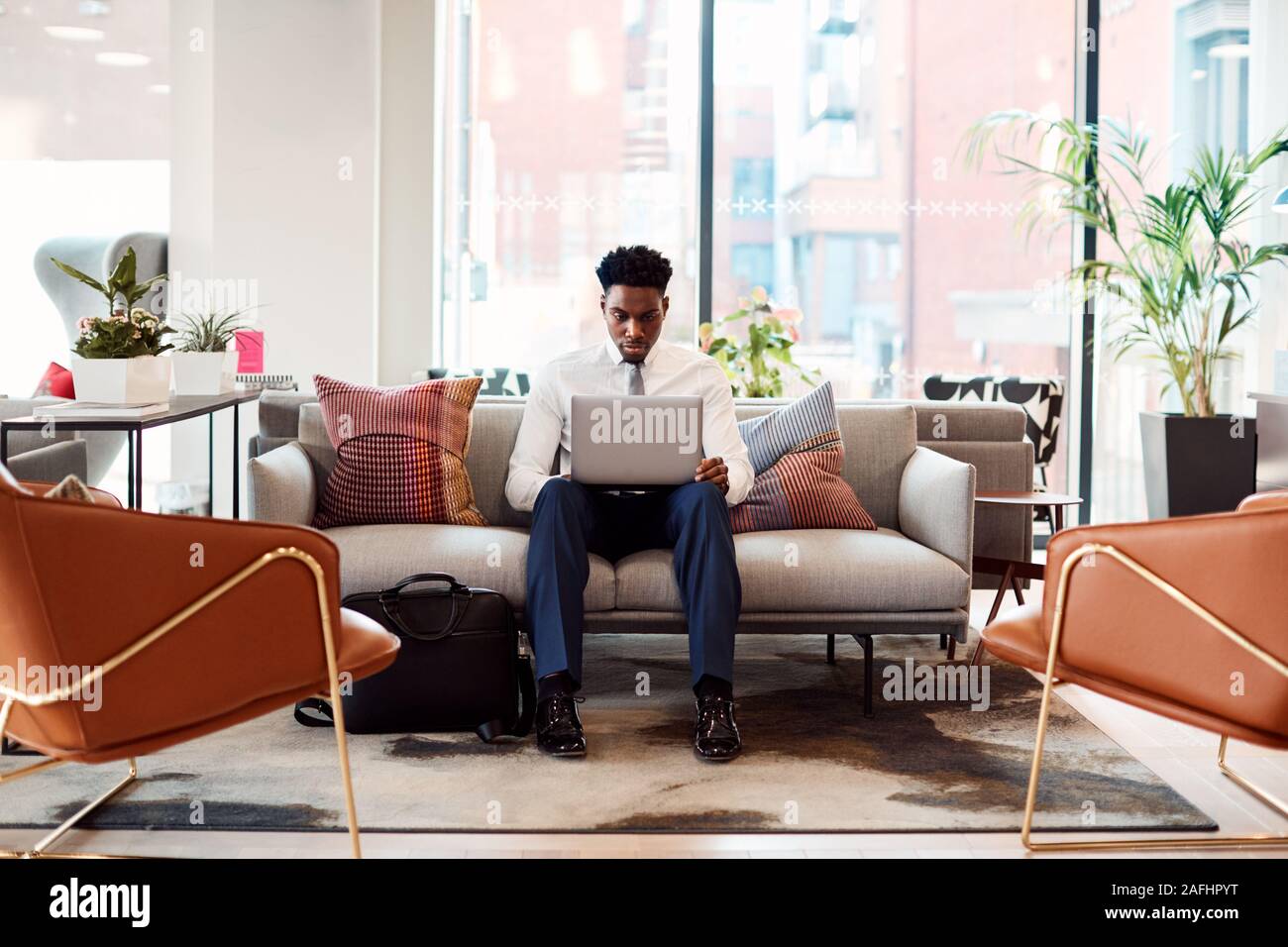 Businessman Sitting On Sofa Working On Laptop At Desk In Shared ...