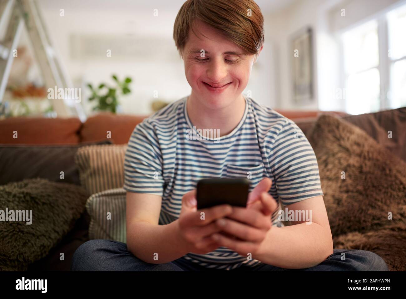 Young Downs Syndrome Man Sitting On Sofa Using Mobile Phone At Home ...