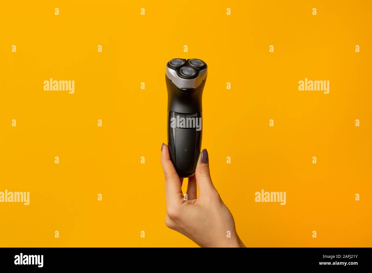 female hand holds a male electric razor on a yellow background. Minimal ...