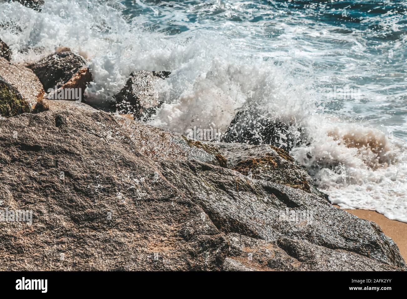 Wave crashing on beach rocks Stock Photo - Alamy