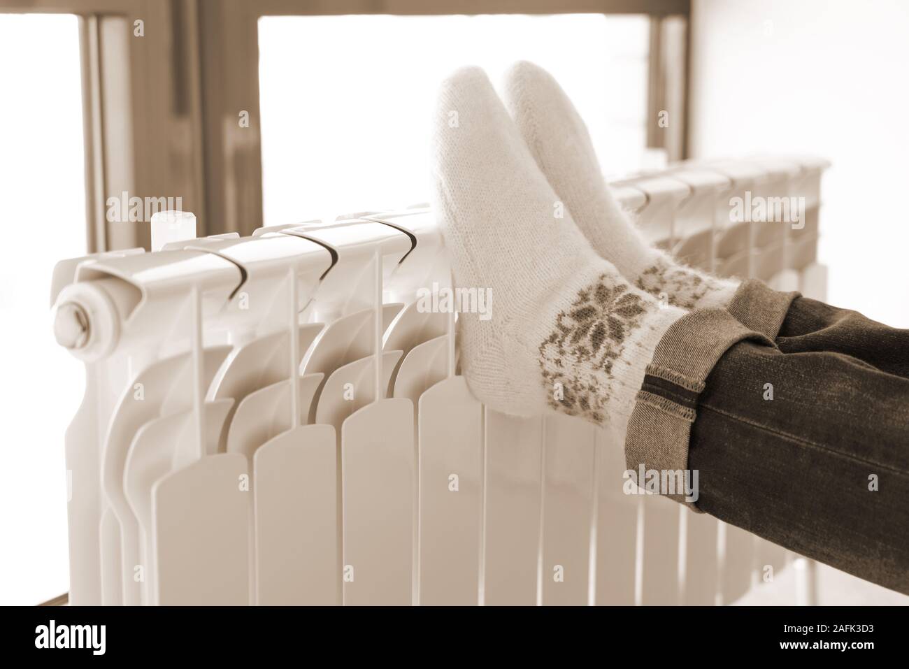 Woman warming up with feet on heater Stock Photo - Alamy