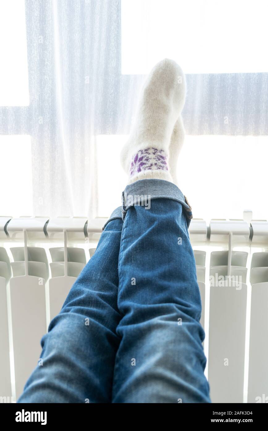 Woman warming up with feet on heater Stock Photo - Alamy