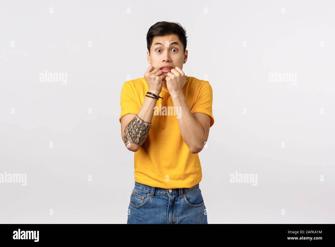 Scared speechless, terrified asian young man with tattoos, wear yellow ...