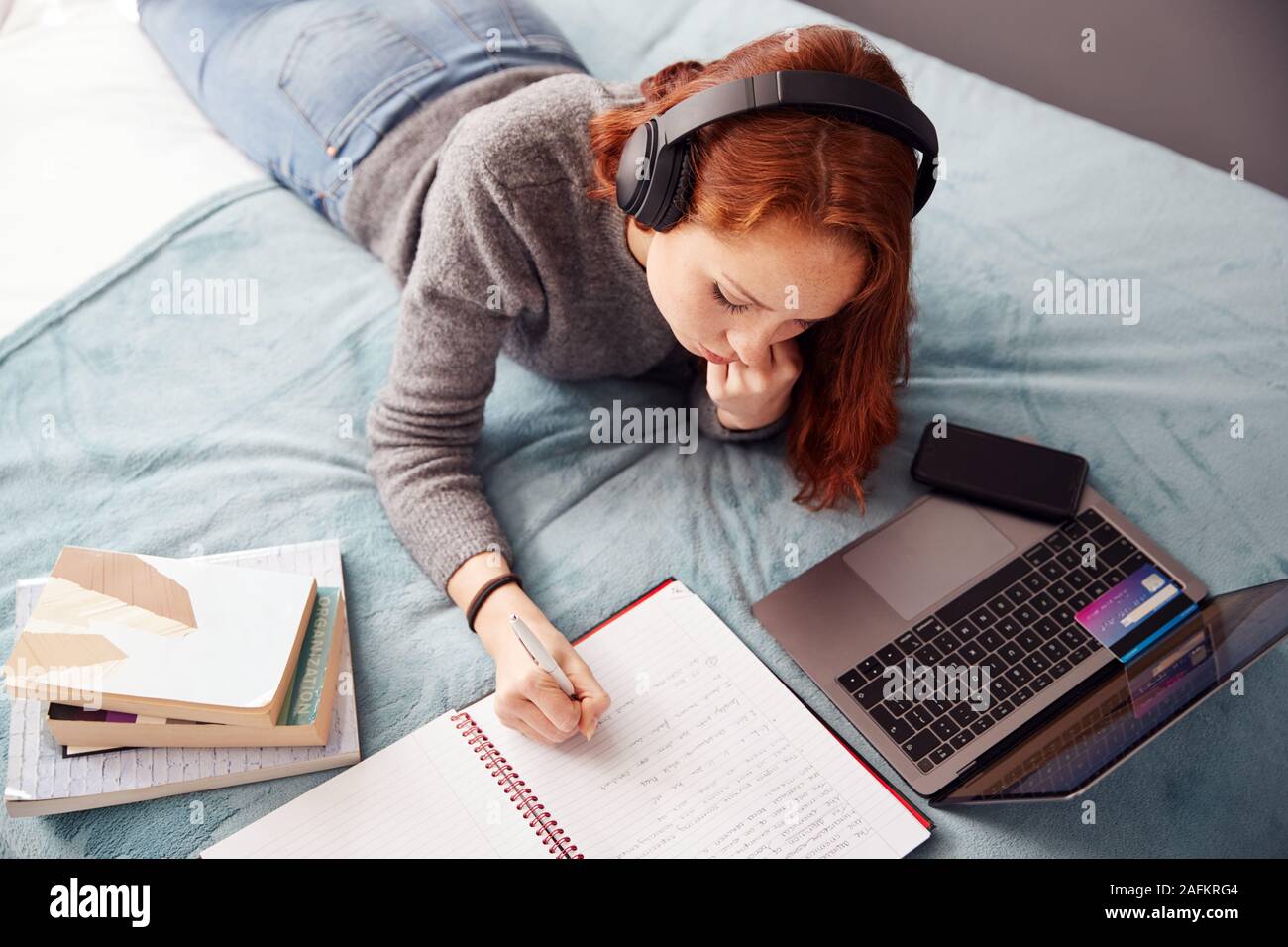 Looking Down On Female College Student Wearing Headphones Lying On Bed ...