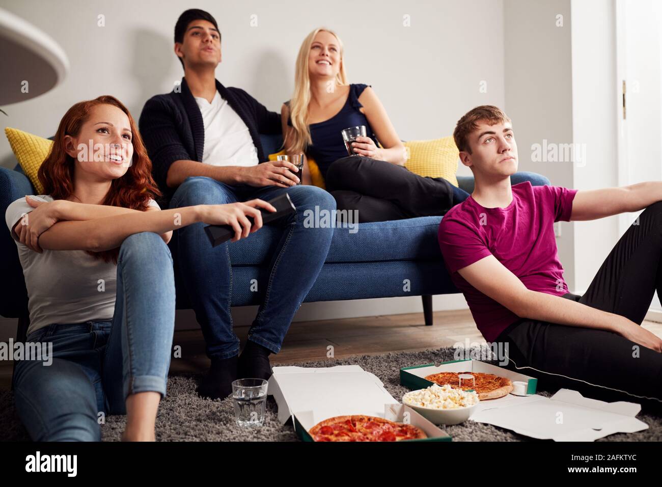 Group Of College Students In Shared House Watching TV And Eating Pizza ...