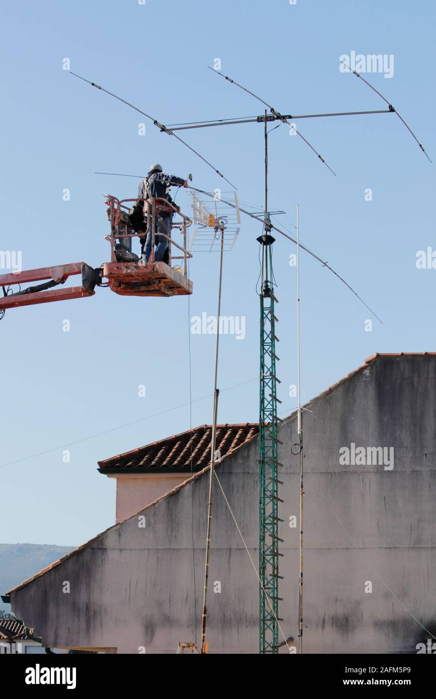 Worker on telescopic elevator repairing a antenna with blue sky on ...