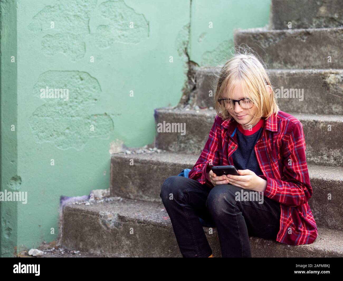 Tween smiling sitting on stairs using smartphone Stock Photo - Alamy