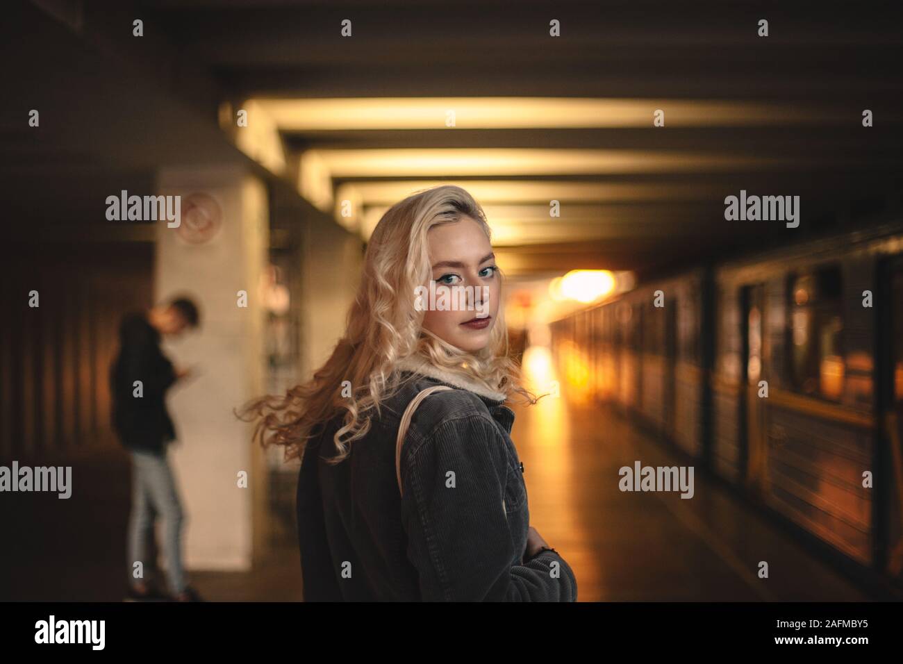 Young woman looking back at camera walking on subway train station ...