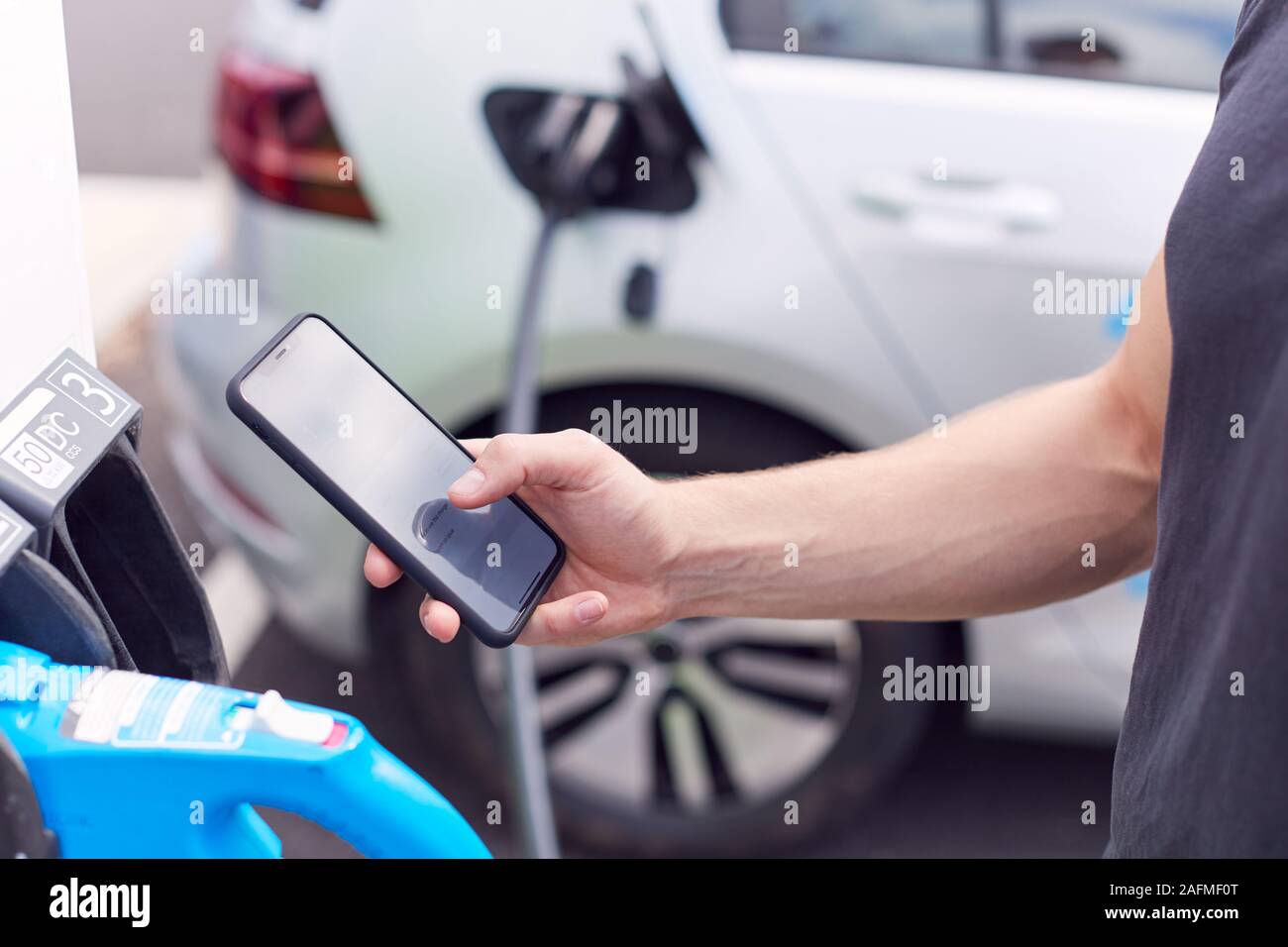 Man Charging Electric Vehicle With Cable Looking At App On Mobile Phone ...