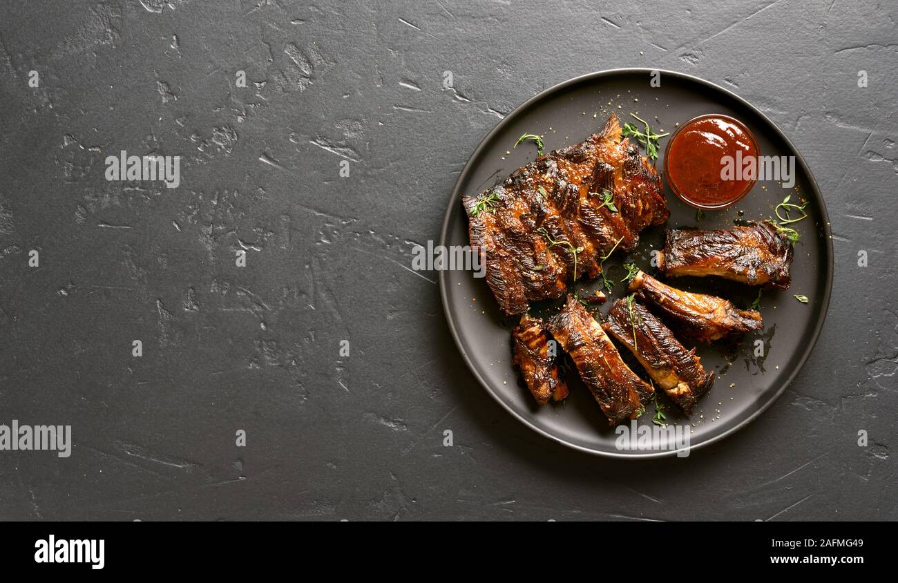 Spicy hot grilled spare ribs on plate over black stone background with ...