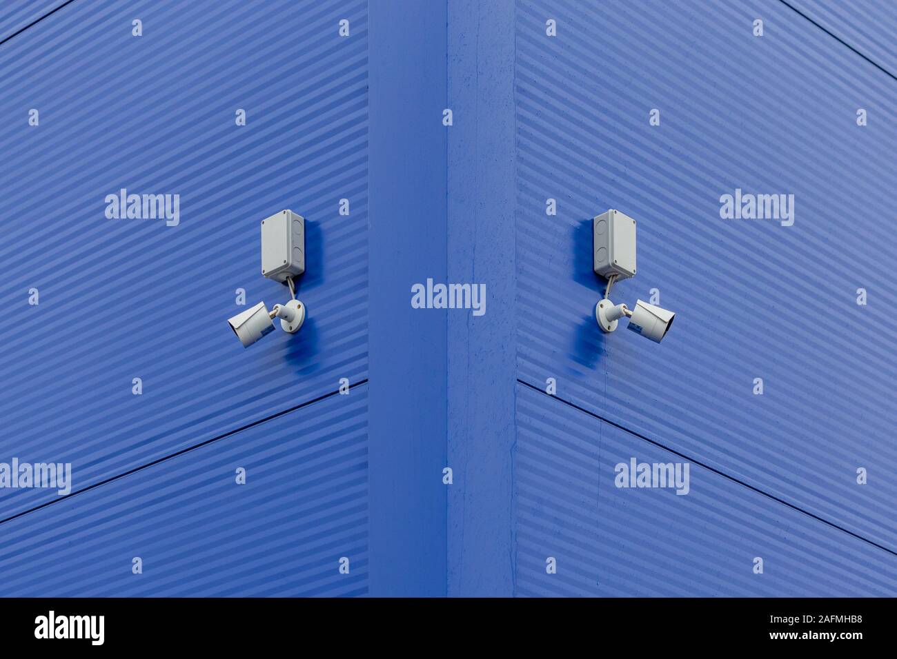 two small white security cameras on blue steel building corner Stock ...