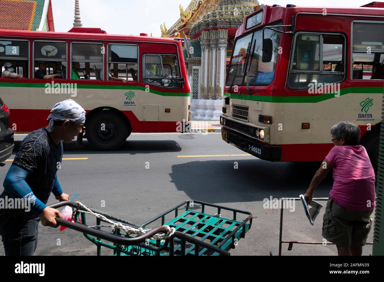 Two buses in street in Bangkok, Thailand, with temple behind. Man with ...