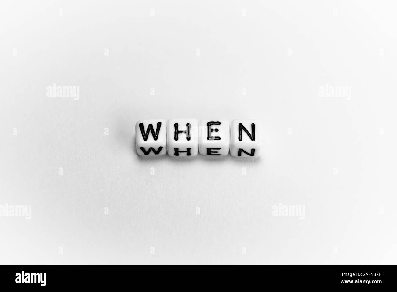 White cubes with question WHEN on white paper background and dark ...