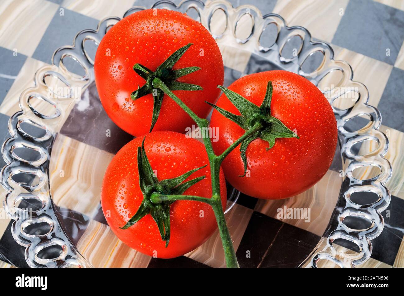 3 Tomatoes on the vine in a glass dish with a checkerboard pattern ...