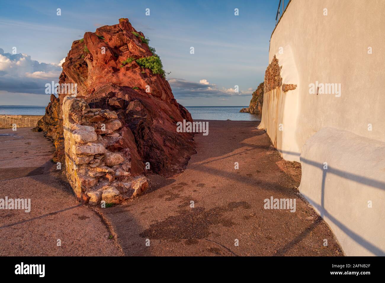 A red rock and a house wall with the sea and clouds in the background ...