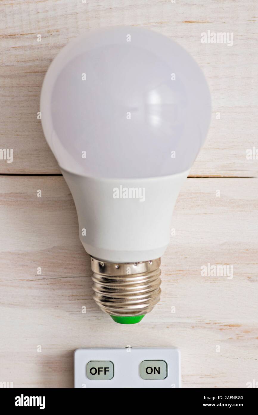 LED light bulb and remote control with buttons on and off on a white ...