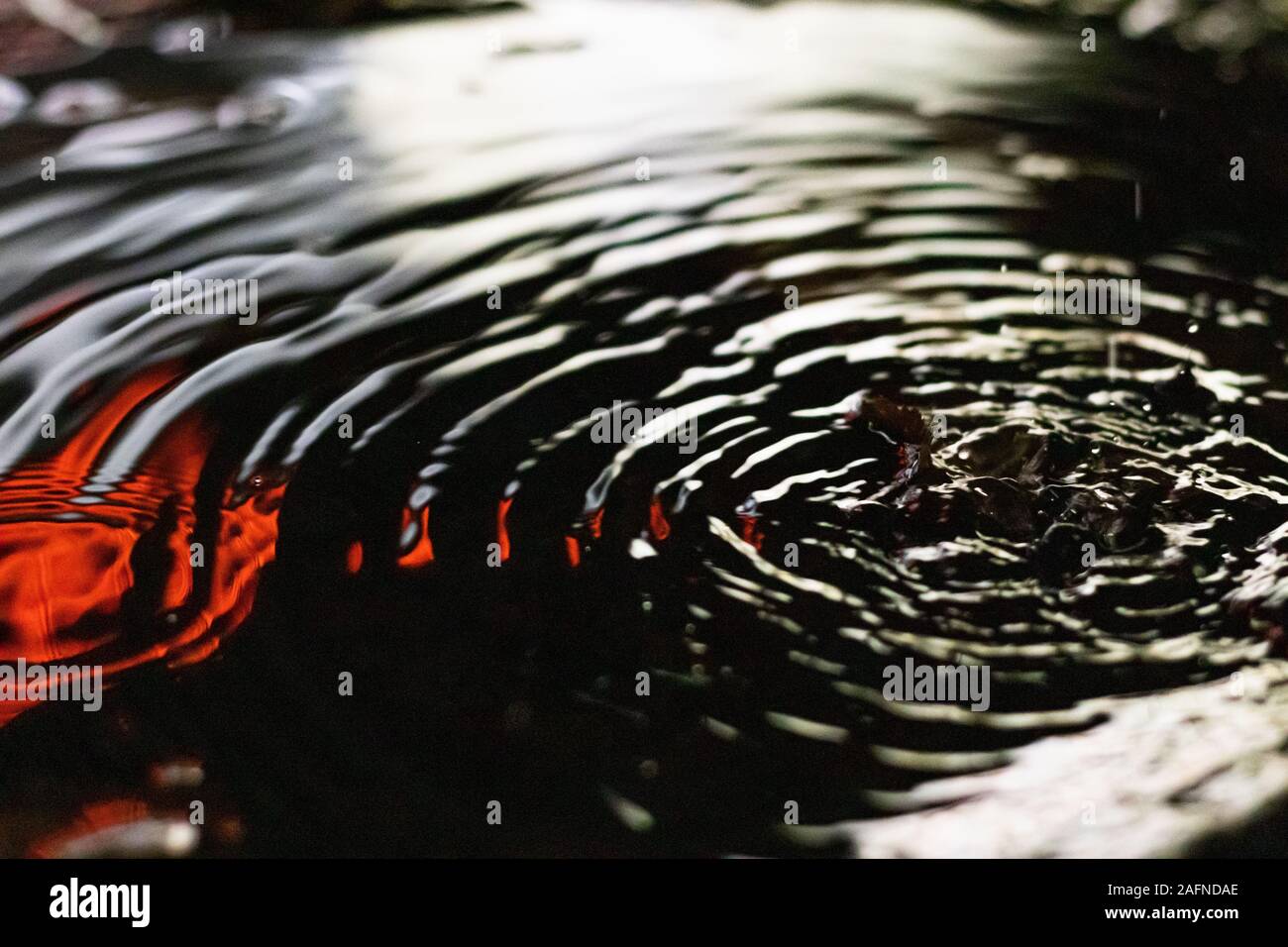 Greyscale shot of raindrops falling on the ground making plashes in the ...