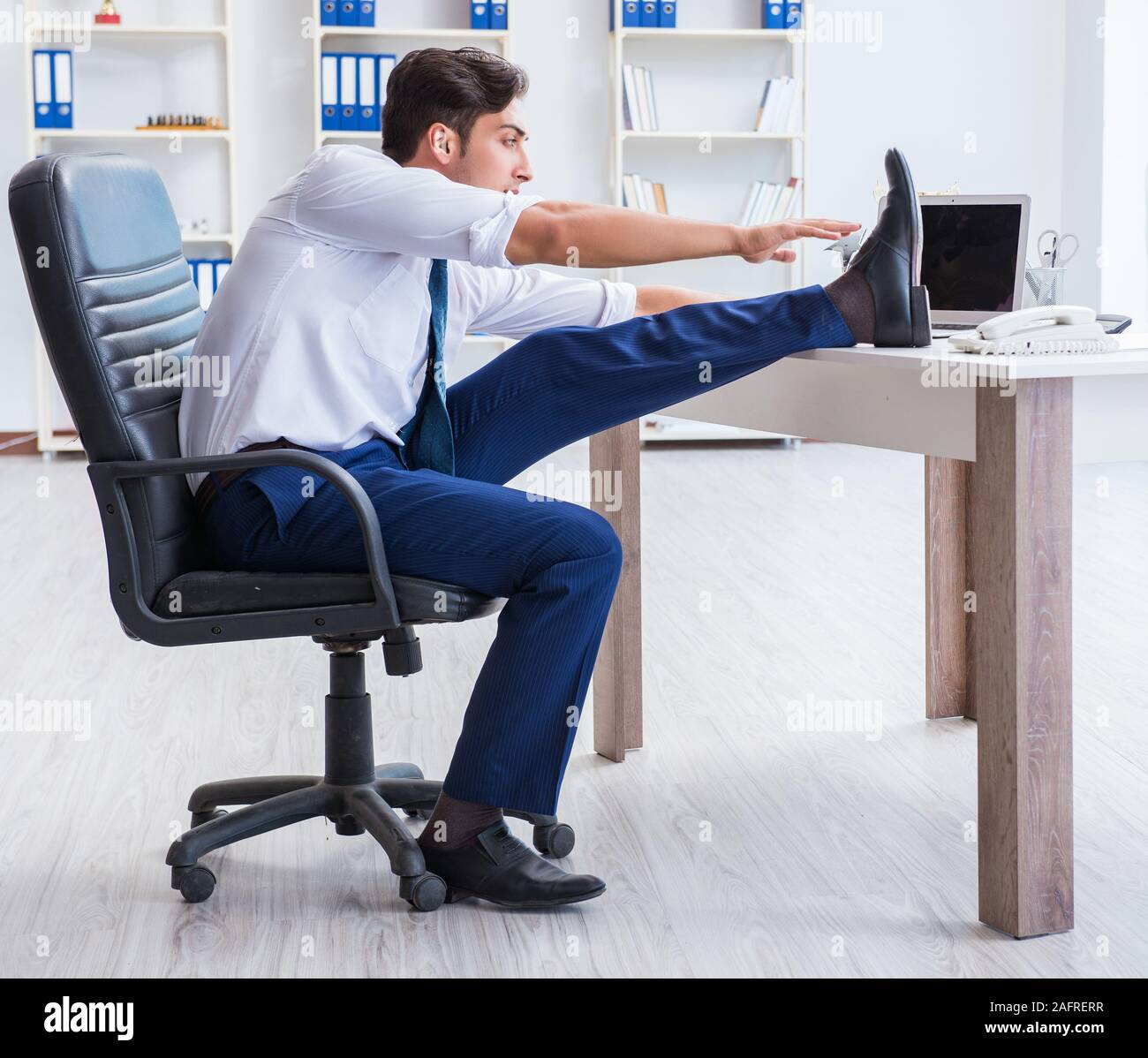 The young businessman doing sports stretching at workplace Stock Photo ...
