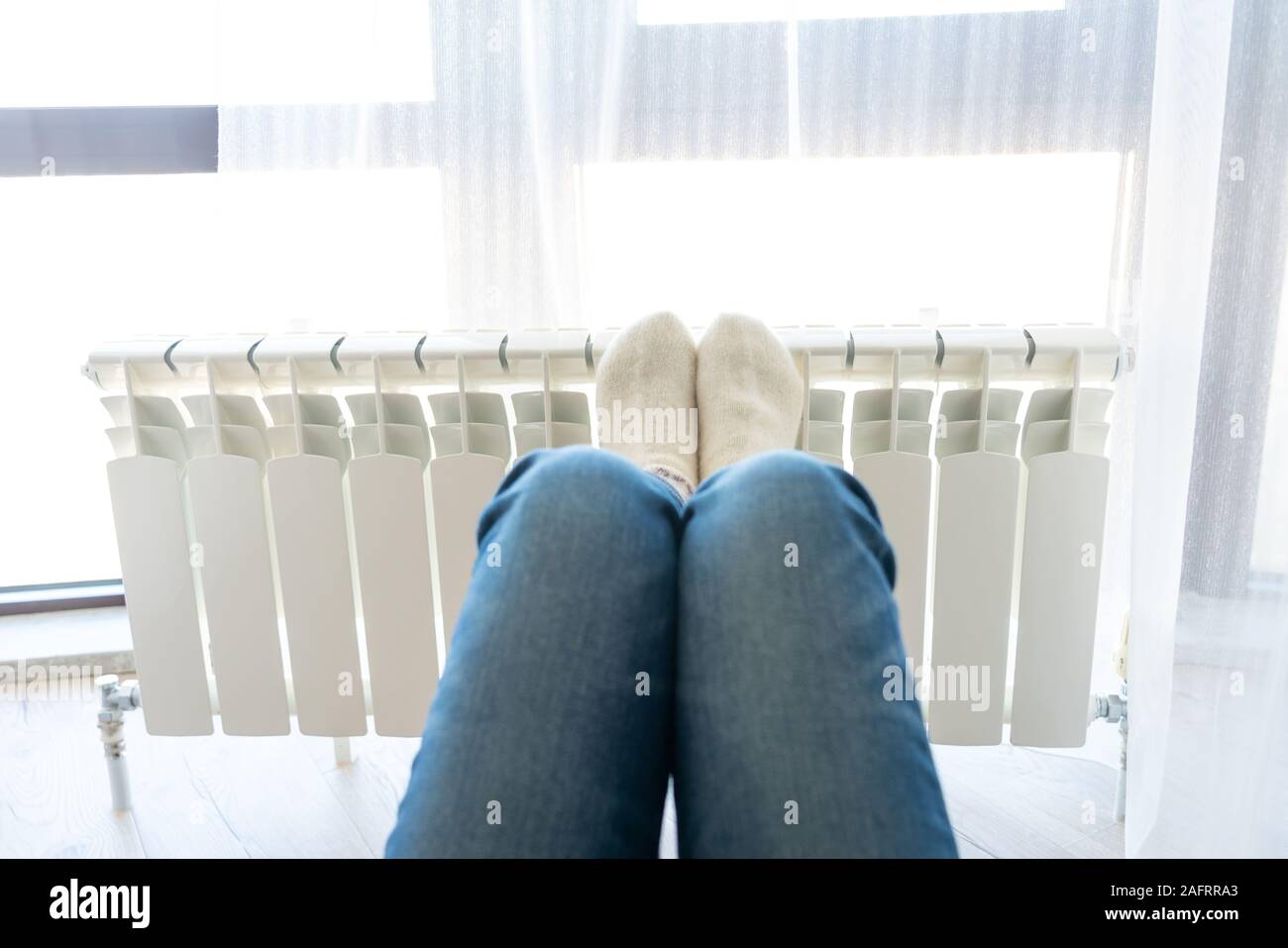 Woman warming up with feet on heater Stock Photo - Alamy