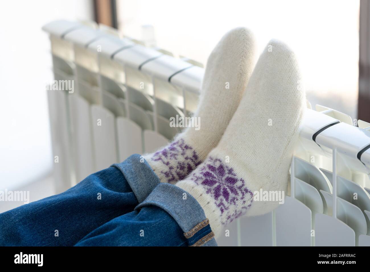 Woman warming up with feet on heater Stock Photo - Alamy