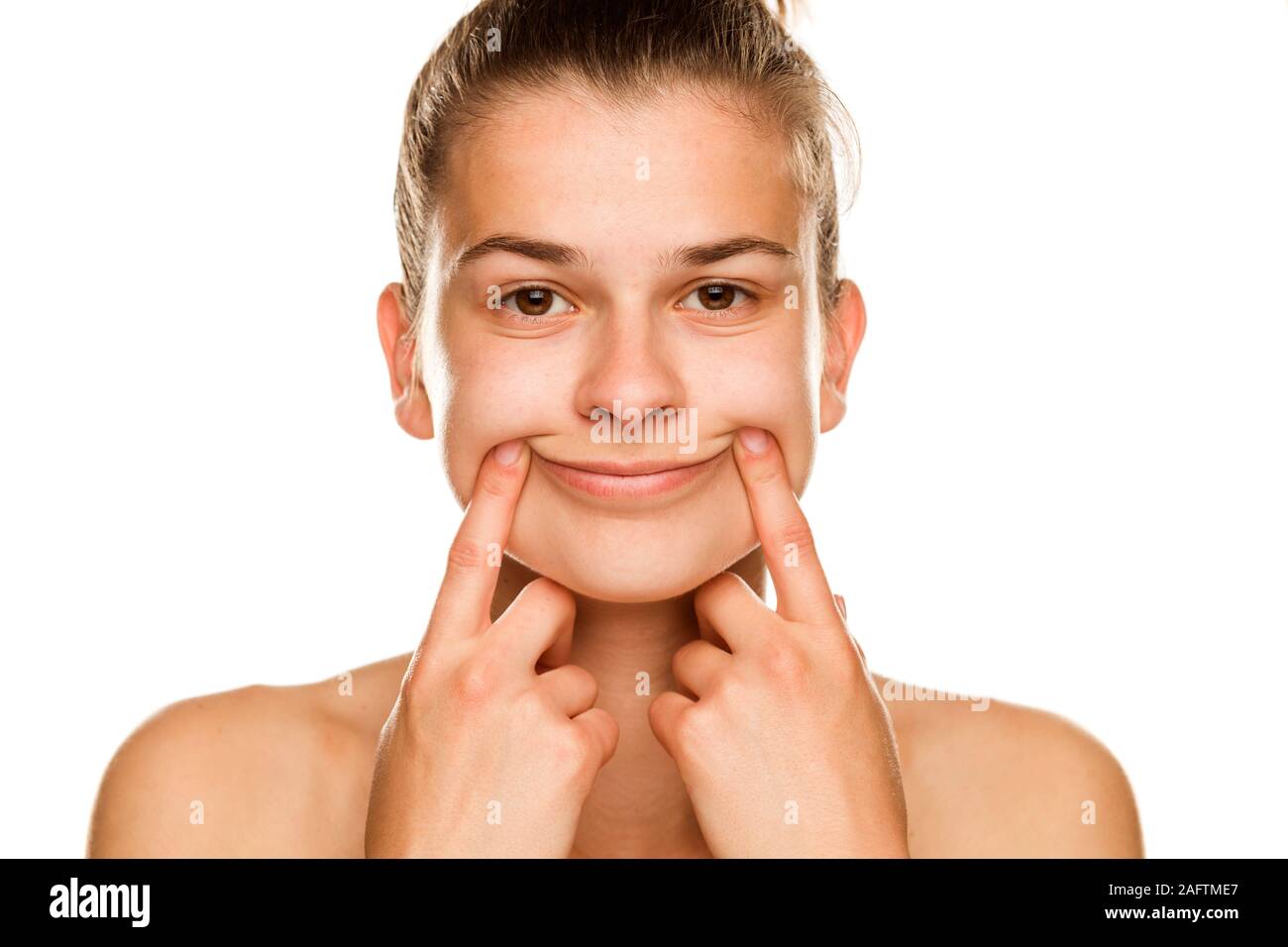 Young woman forcing her smile with her fingers on white background ...