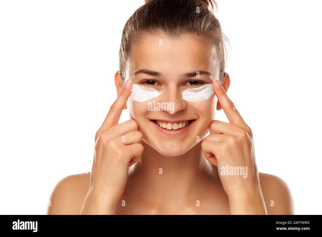 A young woman applying cream under her eyes on white background Stock ...