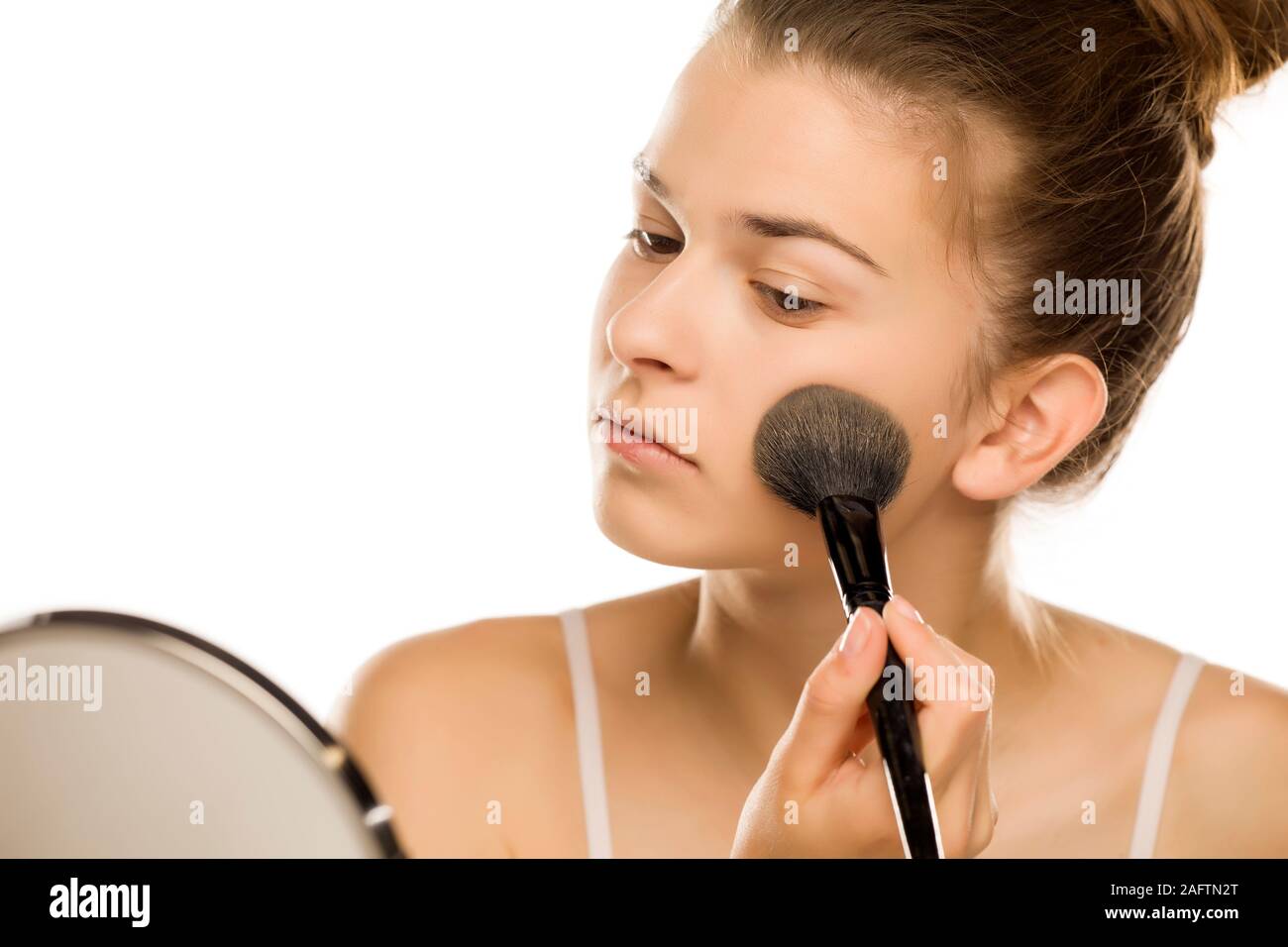 Portrait of young woman applying powder foundation with brush on white ...