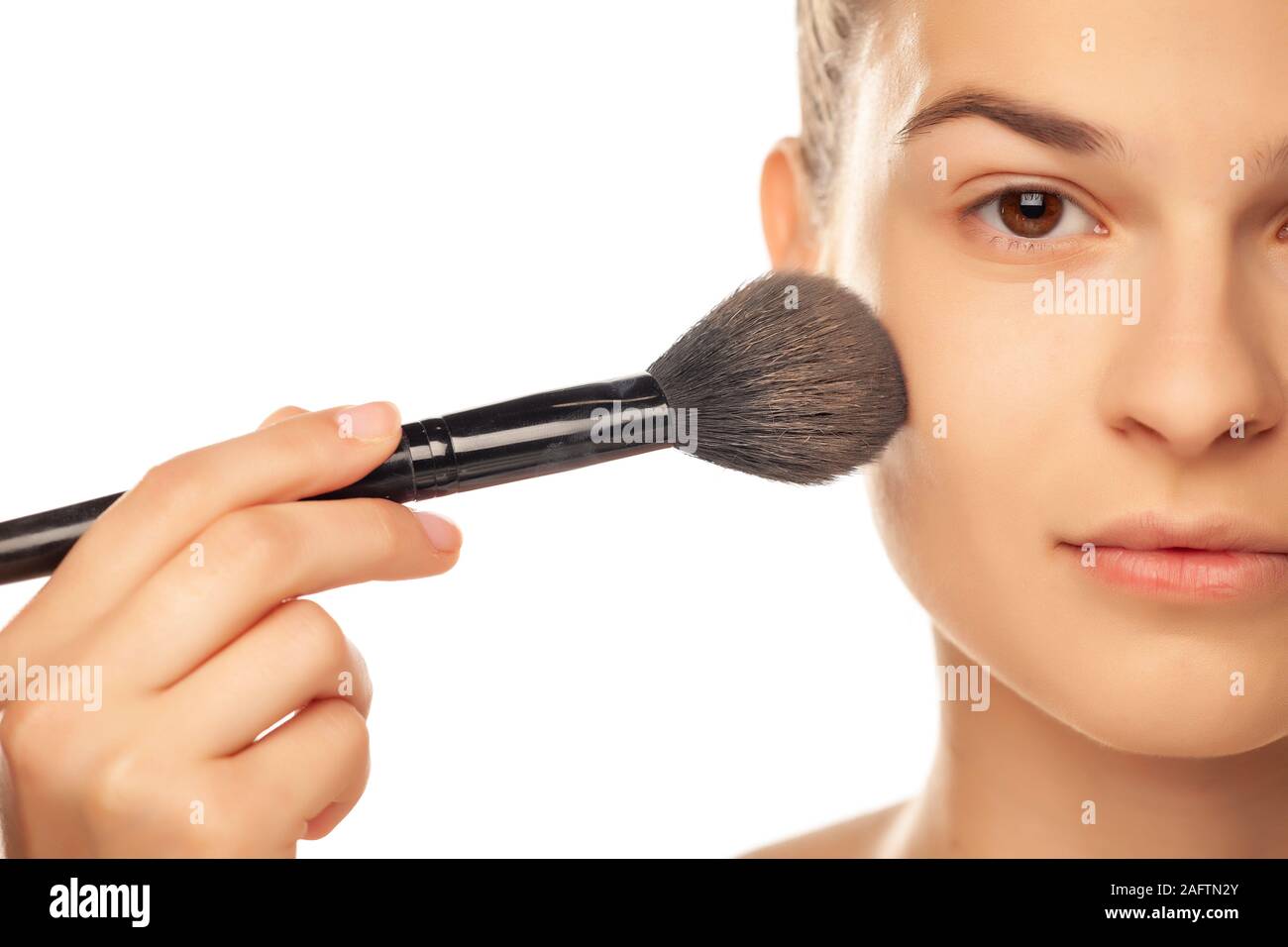 Portrait of young woman applying powder foundation with brush on white ...