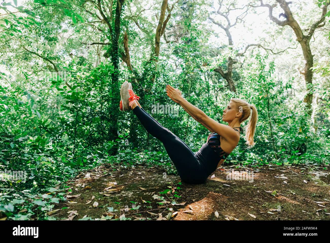 Fit female personal trainer exercising in forest Stock Photo - Alamy