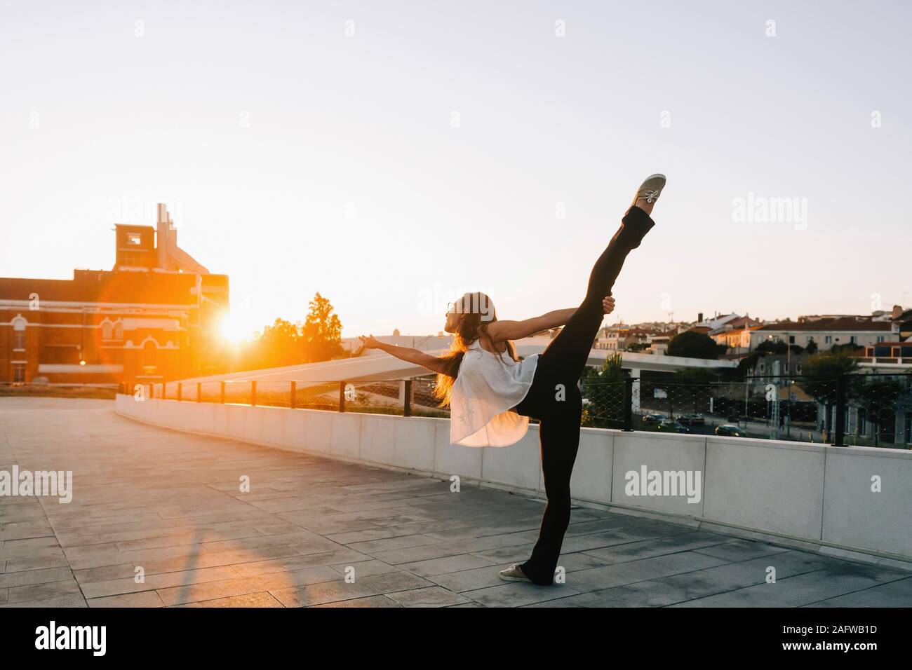 Graceful young female dancer doing standing splits in sunny urban park ...