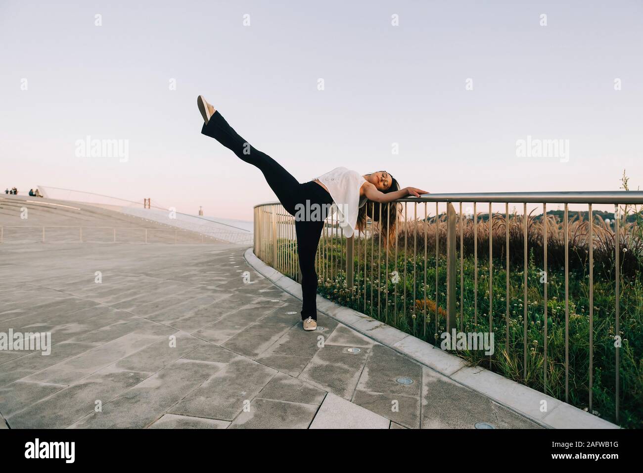 Portrait carefree young female dancer doing standing splits at park ...