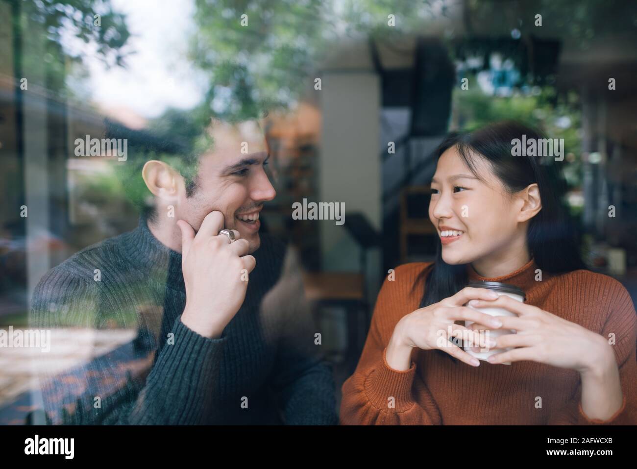 Couple having coffee on a date talking and smile together. shot through ...