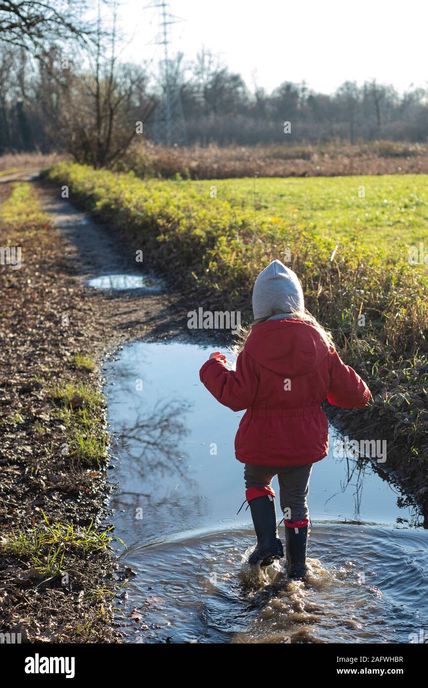 3 years old child splashing in a puddle with red jacket and wellies on ...