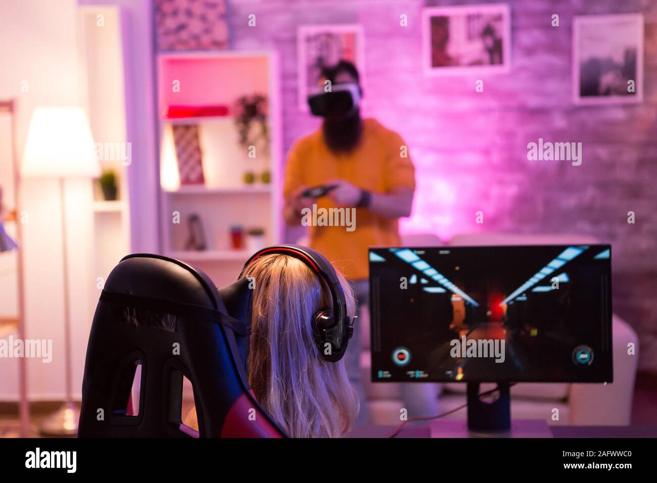 Back view of blond girl playing shooter game sitting on gaming chair ...