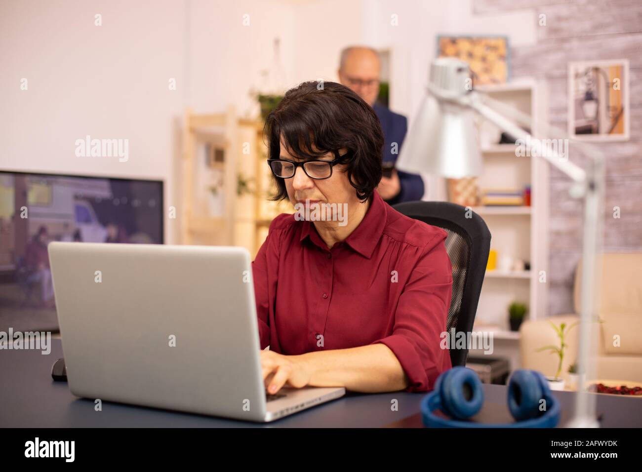 Old woman using a modern computer in her living room while her husband ...