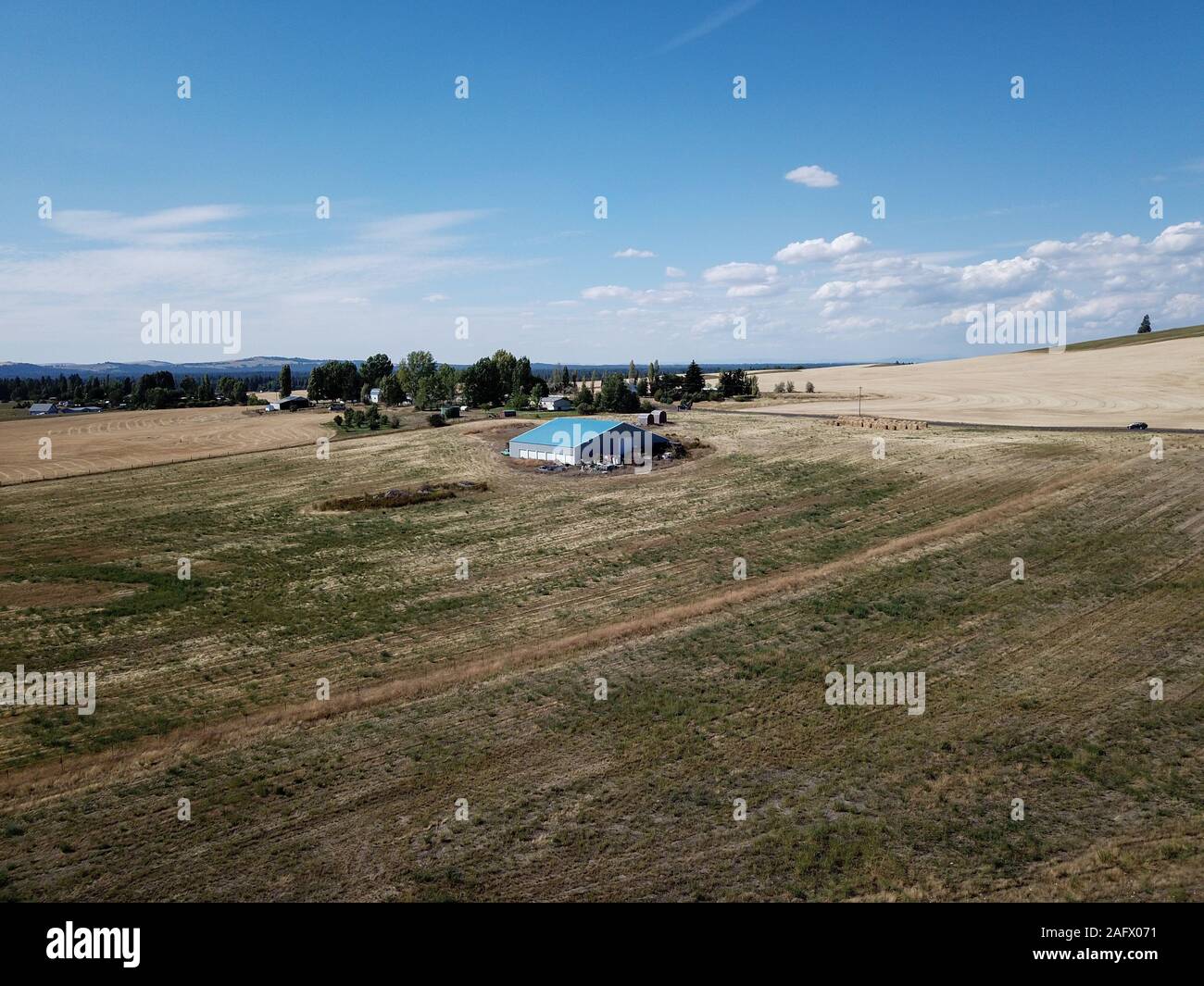 High angle shot of a warehouse in the middle of a field under a blue ...