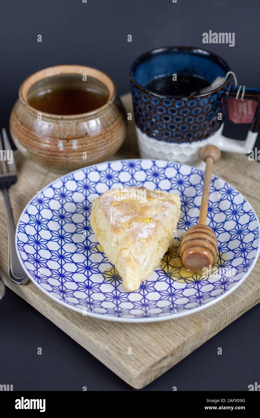 Vertical shot of a scone and honey stick on a plate with a tea on the ...