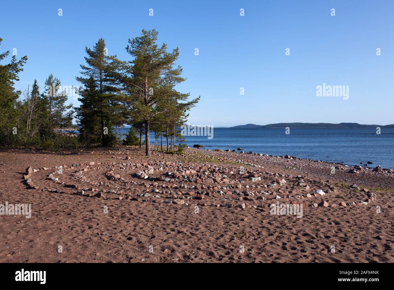 Small labyrinth, maze by the sea. Trees and hills in the background ...