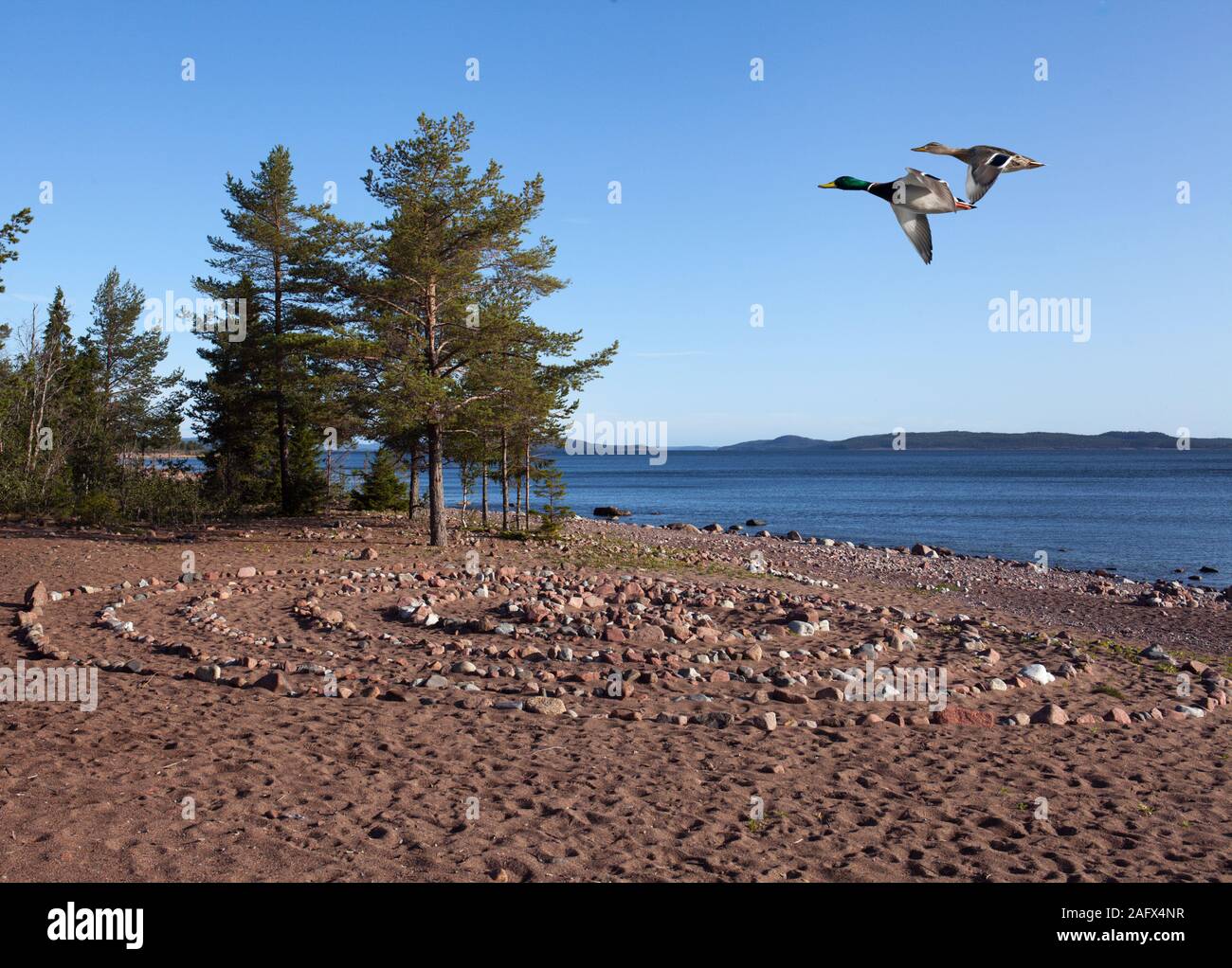 Small labyrinth, maze by the sea. Trees and hills in the background ...