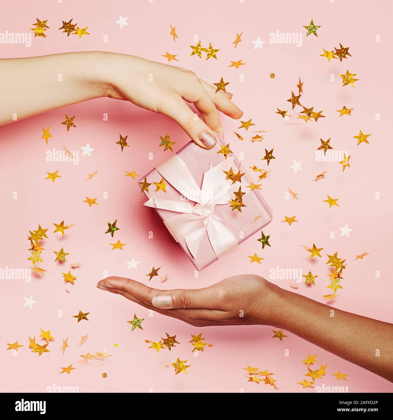 Hand gives a gift and hand takes a gift on pink background with ...
