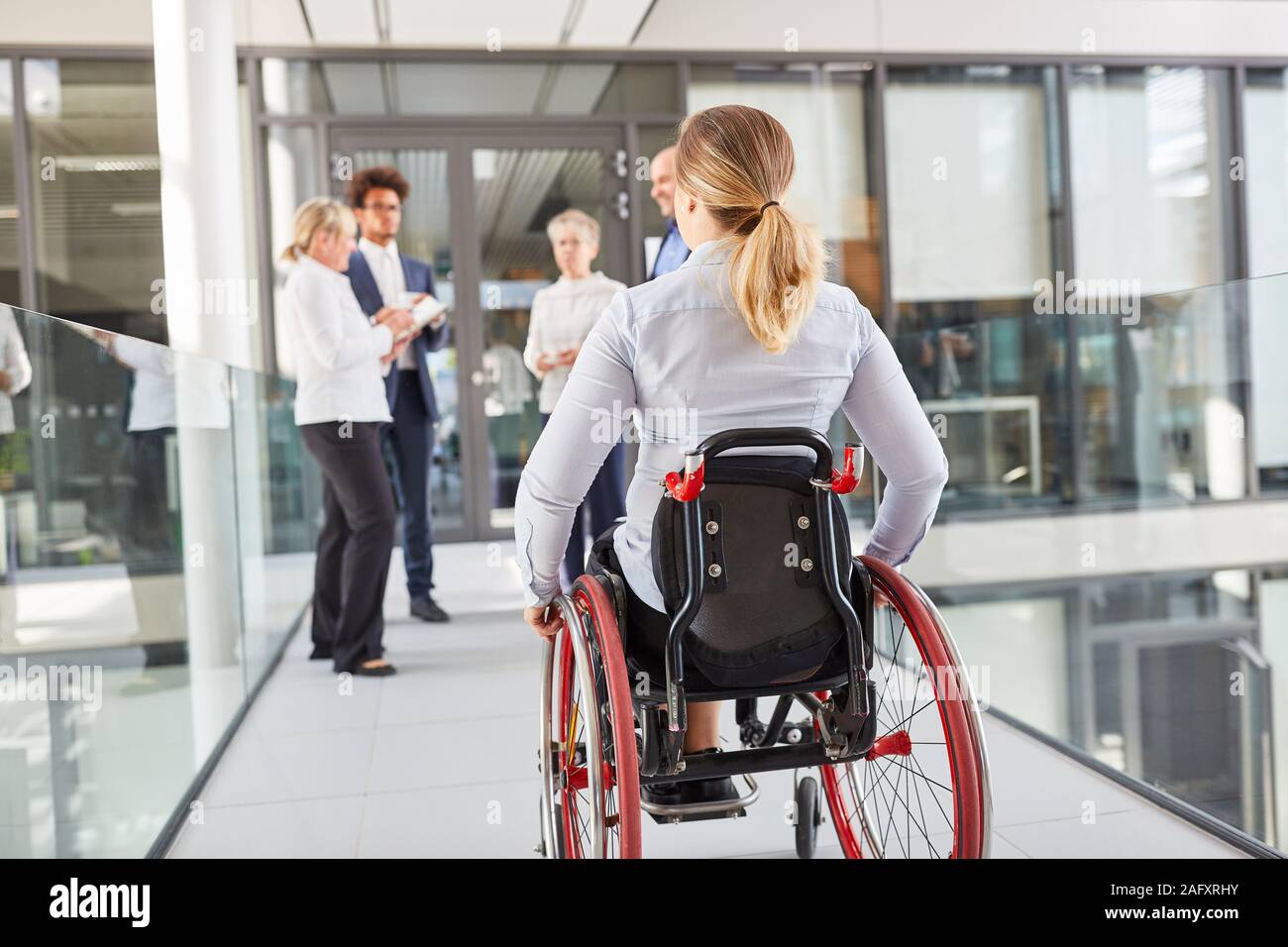 Woman in a wheelchair in the accessible office with business team in ...