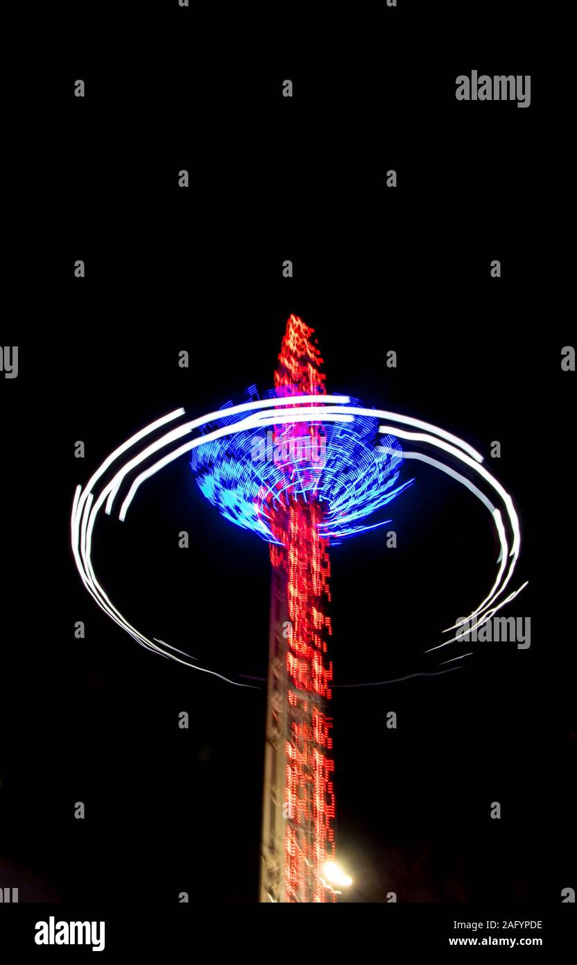 A very large and tall ride at a funfair, light trails seen from the ...