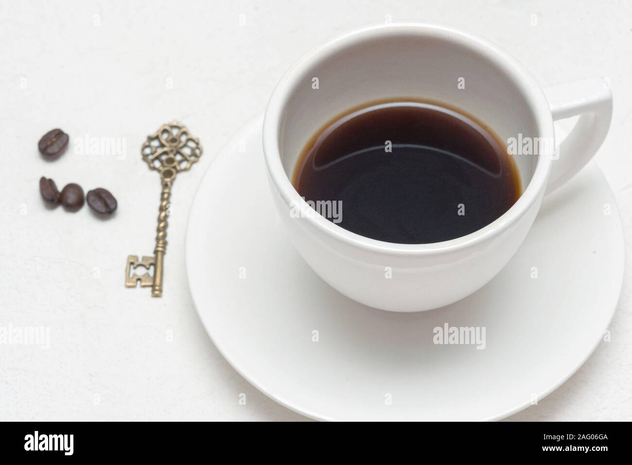 White tea cup with black coffee and golden key on white background ...