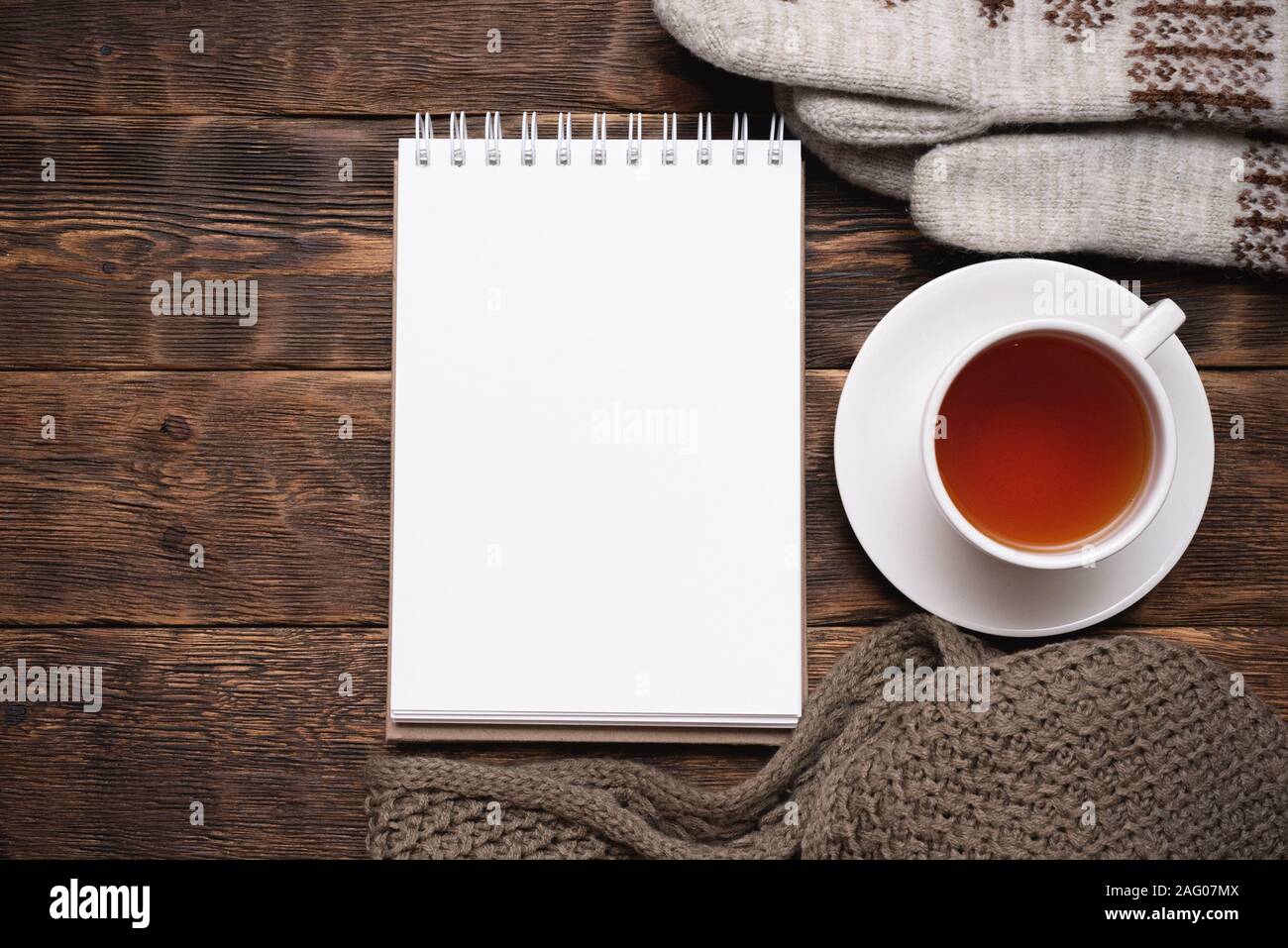 Blank notepad with copy space, warm clothes and cup of tea on brown ...